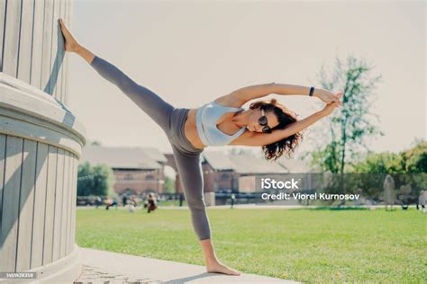 유연한 맞는 여자의 수평 샷은 좋은 신체 모양으로 팔을 제기 와 한쪽 다리 에 서 체조 운동은 야외에서 좋은 날씨를 즐긴다 사람 웰빙 개념 30 34세에 대한 스톡 사진 및