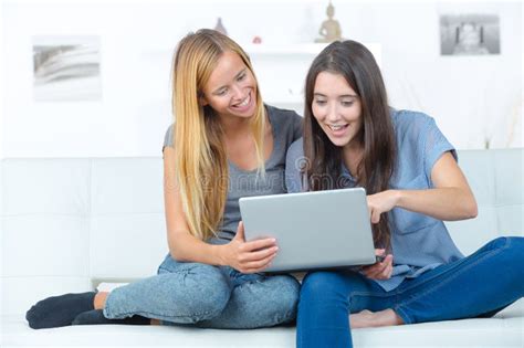 Two Smiling Girlfriends Sitting On Sofa And Doing Homework Stock Image