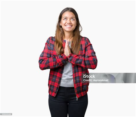 젊은 아름 다운 갈색 머리 여자 구걸 하 고 손으로 얼굴 매우 감정적이 고 걱정에 희망 식 함께 기도 격리 된 배경 위에 자 켓을 입고 용 서에 대 한 요구 종교 개념입니다