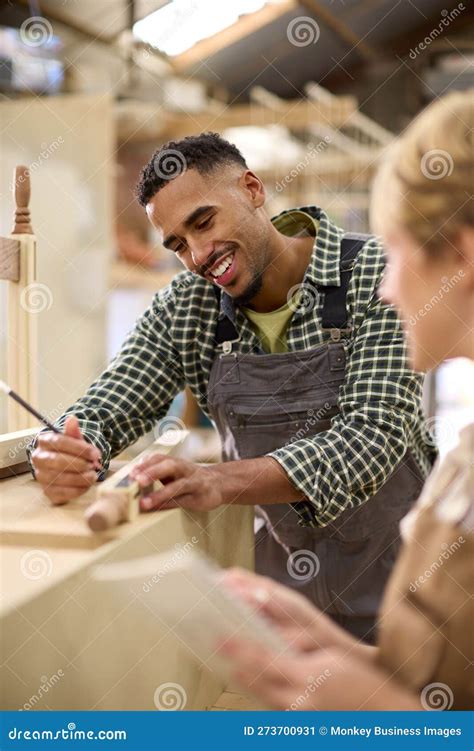 Male And Female Apprentices Working As Carpenters In Furniture Workshop