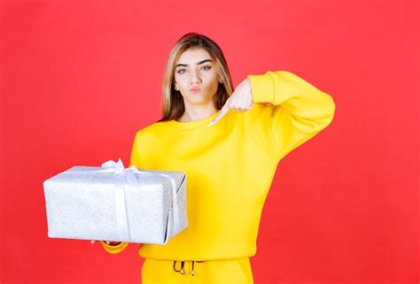 Красивая счастливая девушка держит подарочную коробку на красной стене