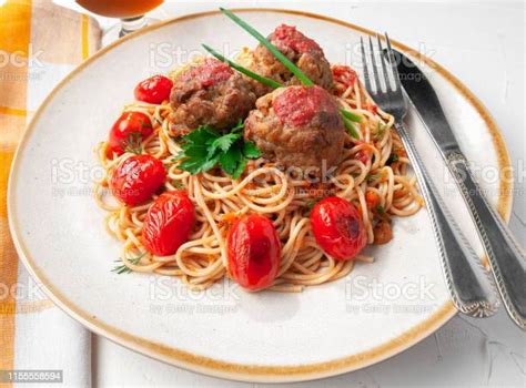 미트볼과 토마토 소스가 들어간 파스타 채소와 구운 체리 토마토로 장식 되어 있습니다 원래 접시에 칼 붙이 위에서 보기 흰색