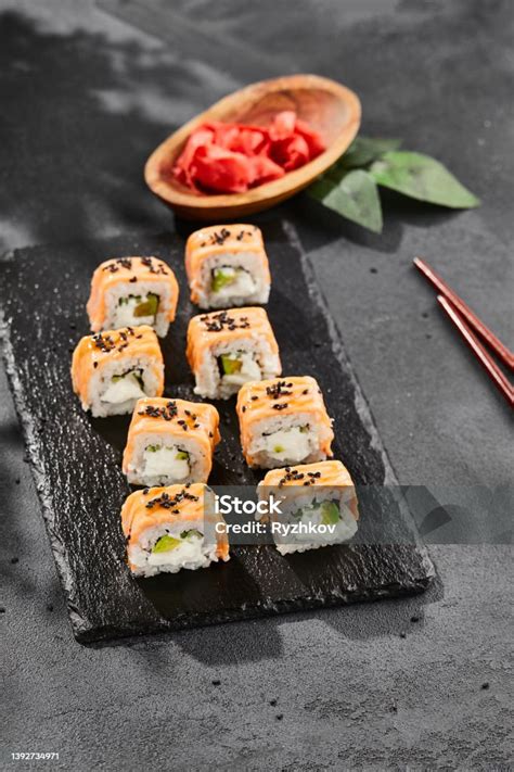 어두운 슬레이트에 마키 초밥 구운 연어와 뜨거운 필라델피아 마키 구운 연어 크림 치즈 아보카도와 함께 스시 롤 블랙 배경 잎 하드 섀도우가 있는 스타일 컨셉 일본어 메뉴 0
