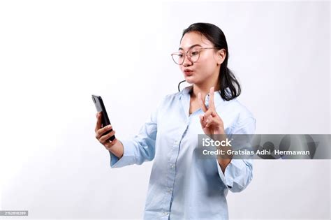 두 손가락을 보여줌으로써 상호 작용 화상 통화를 위해 휴대 전화를 사용하는 정장을 입은 아시아 여성의 초상화 흰색 배경에 고립