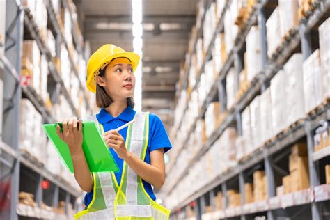 안전 헬멧과 반사 조끼를 착용 아름다운 아시아 엔지니어 여성 그녀는 도자기 집에서 녹색 클립 보드와 선반에 상품과 용품을 확인 물류 및 비즈니스 수출 개념 30 34세에