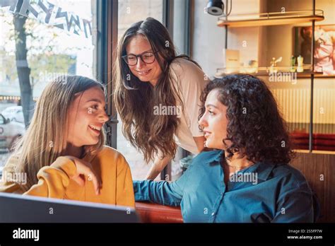 Three Women Smiling Looking Laptop Screen Together Cozy Indoor Setting
