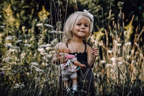 Premium Photo Portrait Of Innocent Girl Holding Doll Amidst Plants On