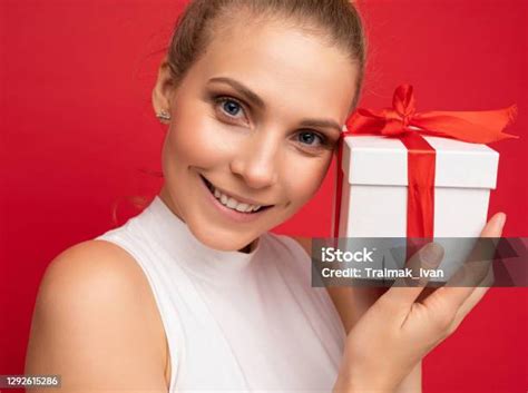 흰색 상의를 들고 선물을 들고 카메라를보고 빨간색 배경 벽에 고립 된 매력적인 행복한 미소 젊은 금발 여성의 초상화 사진 귀여운에 대한 스톡 사진 및 기타 이미지 Istock