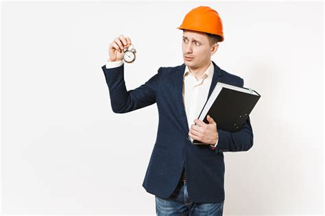 젊은 사업가 검은 양복 보호 Hardhat 들고 종이 문서 및 알람 시계 흰색 배경에 고립 된 검은 폴더에에서 우려 시간이 촉박 합니다 광고에 대 한 남성 노동자입니다