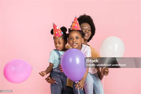 어린 시절 가족 생일 및 축하 개념 생일 모자를 쓰고 행복한 두 명의 어린 아프리카 소녀 분홍색 배경에 어린 예쁜 엄마와