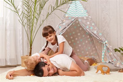 하얀 티셔츠를 입고 아이들과 함께 위그왈 근처 바닥에서 포즈를 취하는 행복한 웃는 남자 아빠와 놀고 웃는 아이들 바닥에 누워