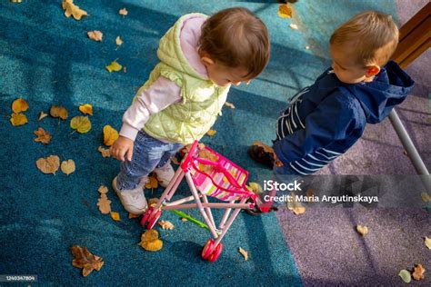 귀여운 유아 소년과 푸른 옷을 입은 아름다운 아기 소녀가 화창한 날에 놀이터의 가을 공원에서 인형을 위해 분홍색 장난감 유모차를 가지고 놀고 있습니다 맨 위 보기 10월에