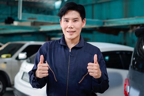 제복을 입은 미소 짓는 잘 생긴 아시아 정비공의 초상화는 차량으로 작업하는 동안 엄지손가락을 치켜들고 자동차 정비사 기술자는