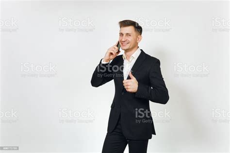 젊은 성공적인 잘생긴 비즈니스 남자가 휴대 전화에 검은 양복에 고립 된 흰색 배경 광고에 대 한 최대 엄지손가락을 보여주는 있다