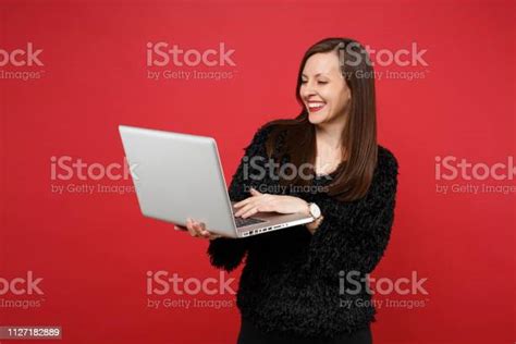 스튜디오에서 밝은 빨간 벽 배경에 고립 된 노트북 Pc 컴퓨터에서 작업 하는 검은 모피 스웨터에 웃는 젊은 여자의 초상화 사람들이 진심으 감정 라이프 스타일 개념 복사