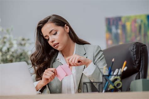 클래식한 메이크업 블레이저를 입은 브라운 긴 머리를 한 아름다운 여성이 사무실 책상에 앉아 노트북 화면을 응시하고 그래픽을 만들고 분홍색 스티커 메모를 벗겨내고 메모를 적어