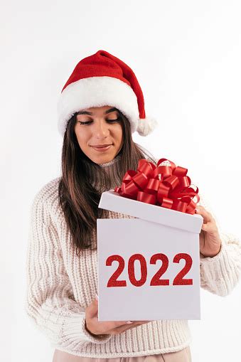 흰색 배경에 젊은 검은 머리 여자는 그녀의 손에 숫자 2022와 선물 상자를 보유하고있다 여자는 산타 클로스 모자와 흰색 스웨터를 입고있다 2022년 새해의 컨셉 2022