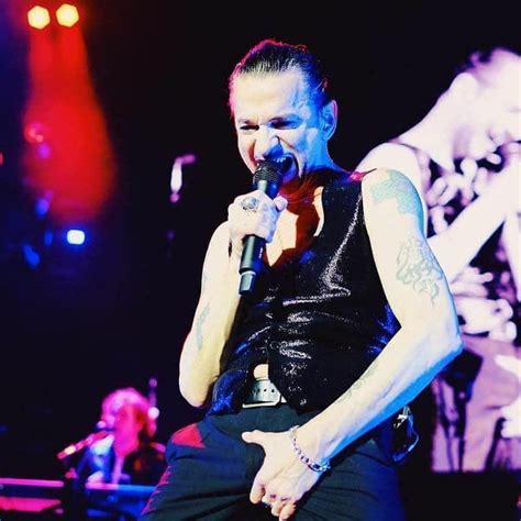 A Man With Tattoos On His Arm Holding A Microphone While Standing In