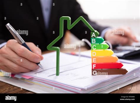 Close Up Of House Model Showing Energy Efficiency Rate In Front Of Businesspersons Hand Using