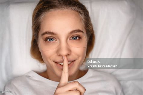 쾌활 한 좋은 젊은 여 자가 흰색 소파에 누워 그녀는 카메라에 똑바로 보고 입에 손가락을 유지 자장 침묵 가꿔주기에 대한 스톡