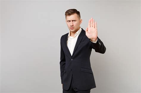 고전적인 검은 양복과 셔츠 스튜디오에 회색 벽 배경에 고립 손바닥 중지 제스처를 보여주는 우려 젊은 비즈니스 사람 성과 경력 부 비즈니스 개념입니다 복사 공간을 비웃는 다