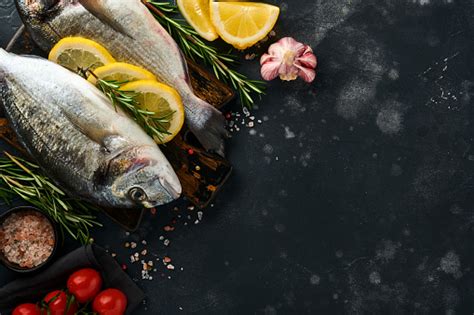 레몬 백리향 마늘 체리 토마토 소금을 검은 슬레이트 돌 또는 콘크리트 배경에 만들기위한 재료로 원시 도라도 신선한 생선이나 도미