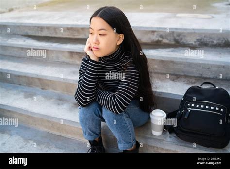 Portrait Of Young Asian Woman With Thoughtful Expression Sitting On