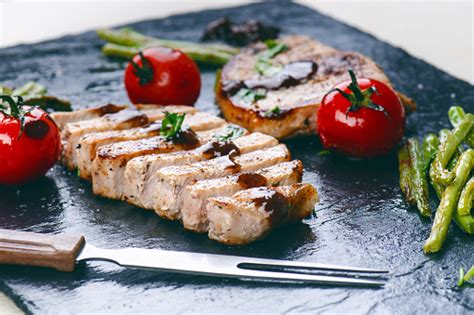 구운된 돼지고기 볶음 야채 토마토 콩 블랙 슬레이트에 소스와 스테이크 거품과 신선한 고기입니다 어두운 배경입니다 구이 및 바베