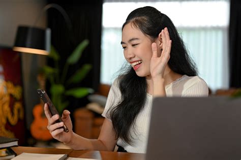 쾌활한 아시아 여성이 손을 흔들며 스마트 폰에서 친구들과 화상 통화를합니다 20 24세에 대한 스톡 사진 및 기타 이미지