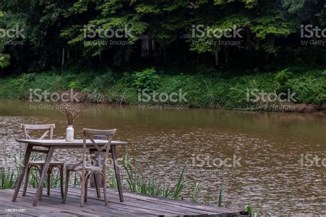 강 옆의 편안한 코너와 오래된 나무 테이블과 나무 의자 2 개를 장식하기 위해 흰색 꽃병에 말린 꽃 0명에 대한 스톡 사진 및