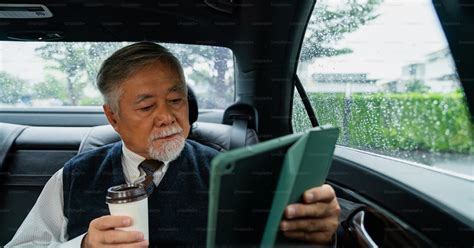 자동차 뒷좌석에 앉아 뜨거운 커피를 마시며 디지털 태블릿으로 사업 계획을 읽는 동안 자신감 있는 수석 사업가 자동차 운전에 종사하는 고령 임원 Ceo 사무실 출근 사진
