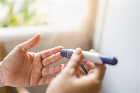 아침에 포도당 측정기로 혈당 수치를 확인하기 위해 손가락에 랜싯을 사용하여 여성의 손을 닫습니다 의학 당뇨병 당혈증 건강 관리