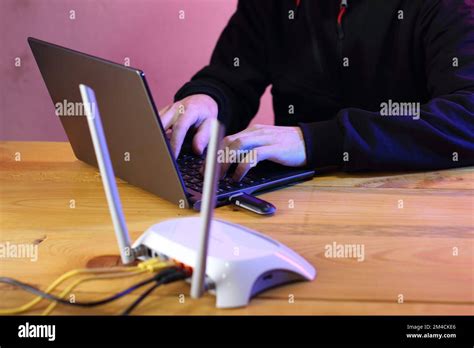 a person typing on a laptop with a modem connected and a blurred router