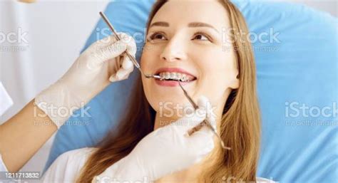 치과 진료소에서 치과 의사가 검사 한 치열 교정 브래킷을 가진 미소 짓는 젊은 여성 건강한 치아와 의학 개념 건강 진단에 대한