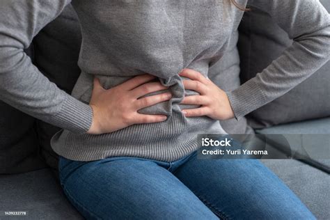 집에서 소파에 앉아 있는 젊은 여성의 클로즈업 건강에 해로운 소녀는 식중독 복통 및 결장 문제 위염 또는 설사로 고통받습니다
