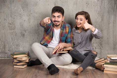 Jovem casal sentado no chão livros e apontando para a frente Foto