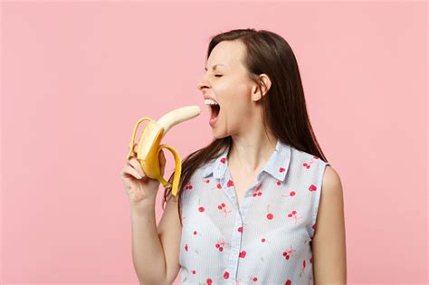 눈을 유지 하는 여름 옷에 미친 젊은 여자는 스튜디오에서 분홍색 파스텔 배경에 고립 된 신선한 잘 익은 바나나 과일을 물고 사람들은 생생한 라이프 스타일 휴식 휴가