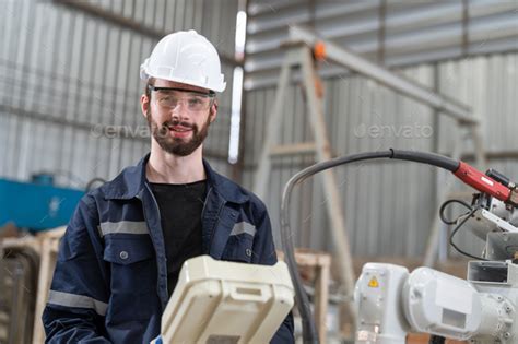 Male Automation Engineer Using Remote Controller Control Robot Arm Welding Machine In Factory