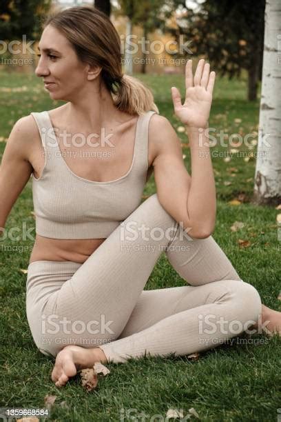 베이지 색 상의와 레깅스를 입은 중년의 금발의 백인 여성 운동선수는 도시 공원에서 요가 아사나스를 연습합니다 조화와 평화 야외