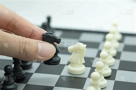 棋盘游戏，商业和规划概念。男人的手握和移动黑色的象棋骑士棋子在排在棋盘上的白子前面。素材 花瓣网