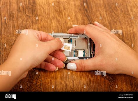 The Insertion Of The SIM Card In A Smartphone On Wooden Table Girl S Hands Insert SIM Card In