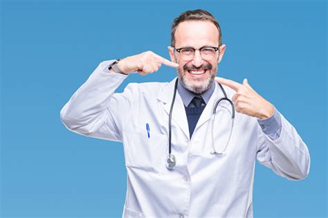 중 년 수석 노인의 의사 남자 착용 의료 유니폼 웃 고 자신감 보여주는 손가락 치아와 입 지적 배경 고립 건강 개념입니다