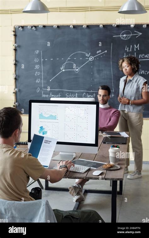 Young Economist Analyzing Graphs On Computer Screen On Background Of Two Biracial Colleagues
