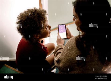 Son Looking At Mother Holding Smart Phone With Home Automation App