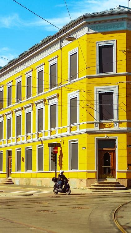 노란색 건물 근처에서 모터 스쿠터를 타고 있는 남자 · 무료 스톡 사진
