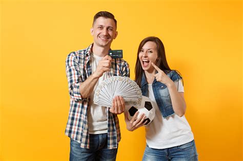 젊은 승 커플 여자 사람 축구 팬 들의 달러 돈 신용 카드 축구공 번들을 들고 노란색 배경에 고립 된 지원 팀을 응원 합니다 스포츠 베팅 열정 가족 라이프 스타일 개념입니다