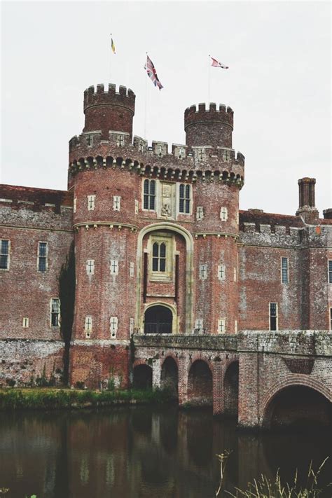 An Old Brick Castle With A Bridge Over The Water And Two Flags Flying Above It