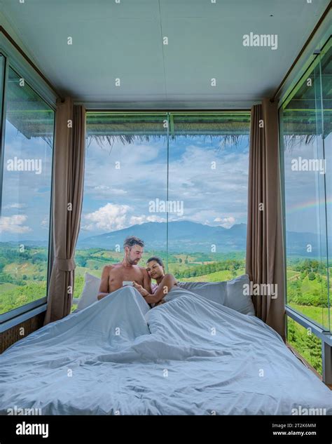 A Couple Of Men And Women Laying In Bed With Open Widows Looking Out