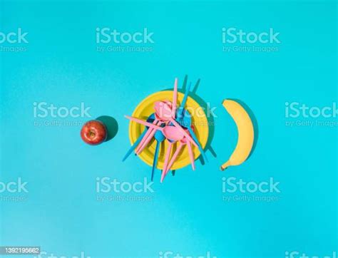 파란색과 분홍색 플라스틱 숟가락과 사과와 바나나가있는 노란색 플라스틱 접시가 파란색 배경에 있습니다 최소한의 개념 개념에 대한
