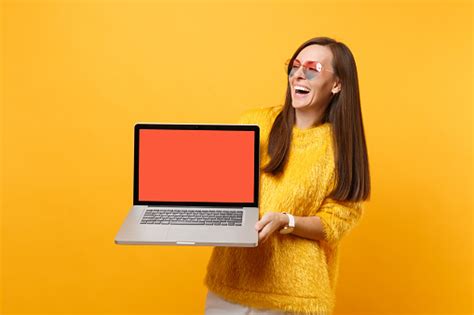 밝은 노란색 배경에 고립 된 빈 검은색 빈 화면으로 노트북 Pc 컴퓨터를 들고 심장 안경에 젊은 여자를 웃 고 있다 사람들이